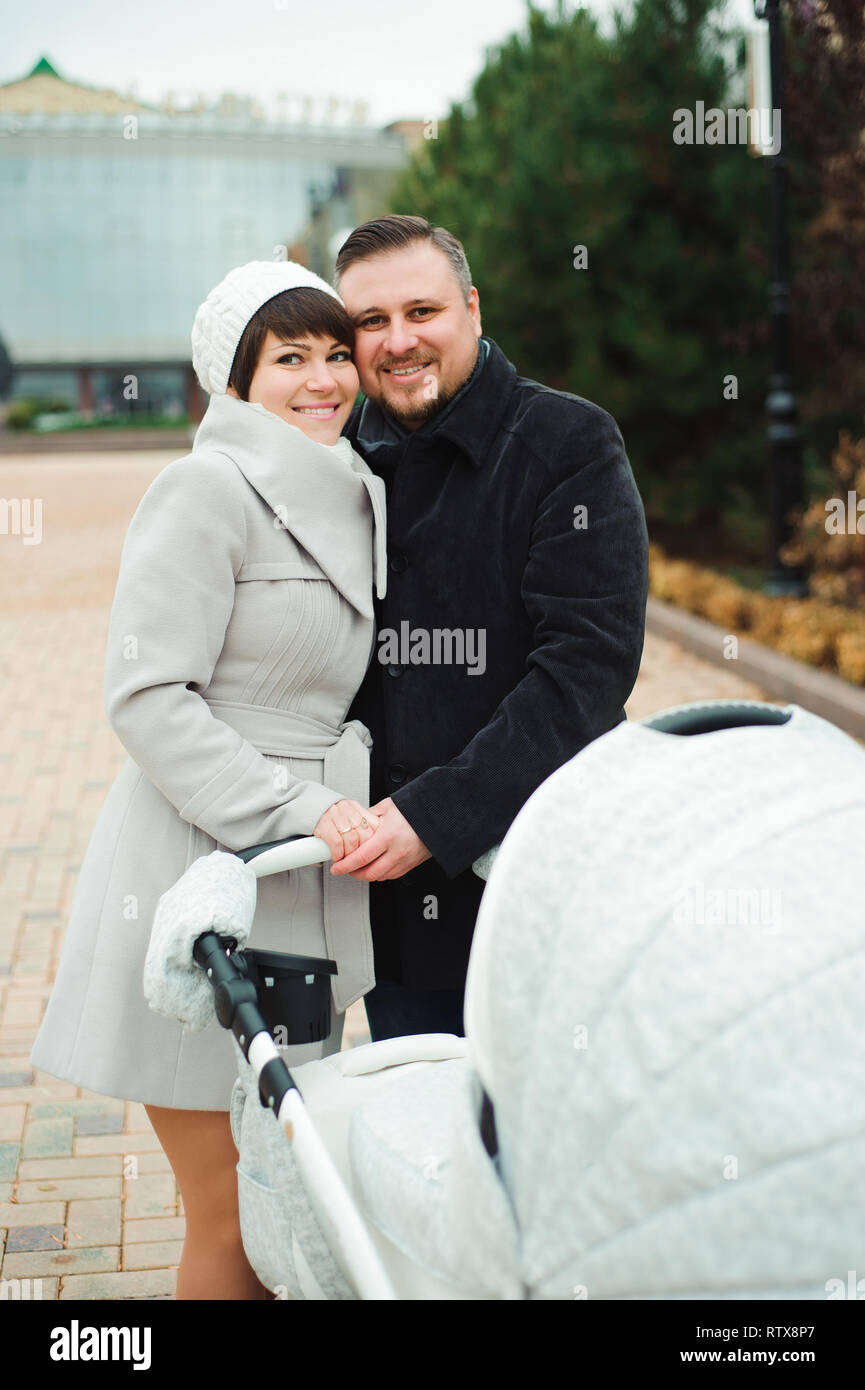 Family walk in the autumn park with a pram. Mom, dad and baby outdoors ...