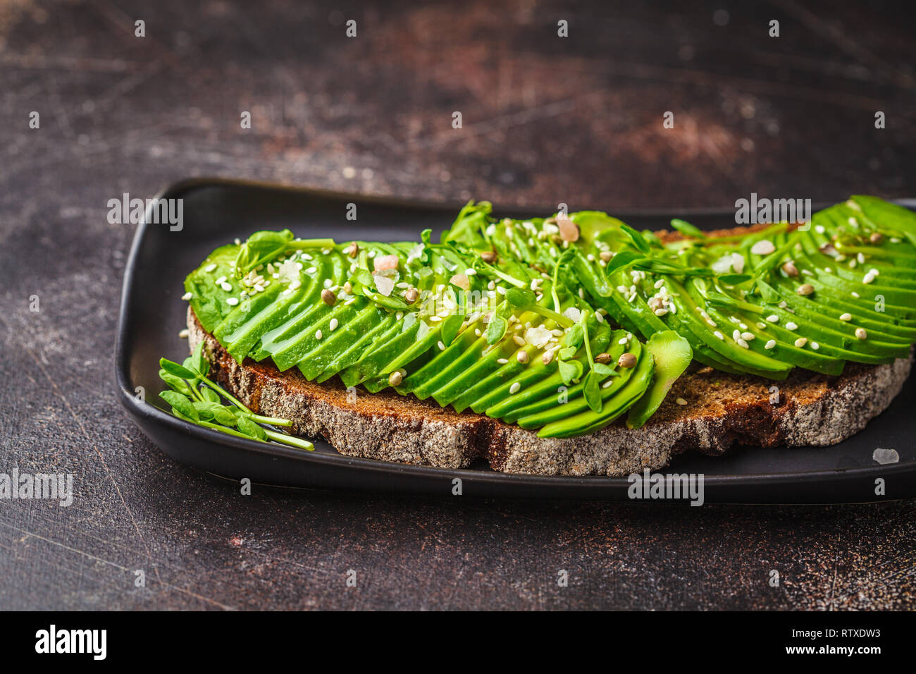 Avocado toast with rye bread and seeds on a black plate, dark ...