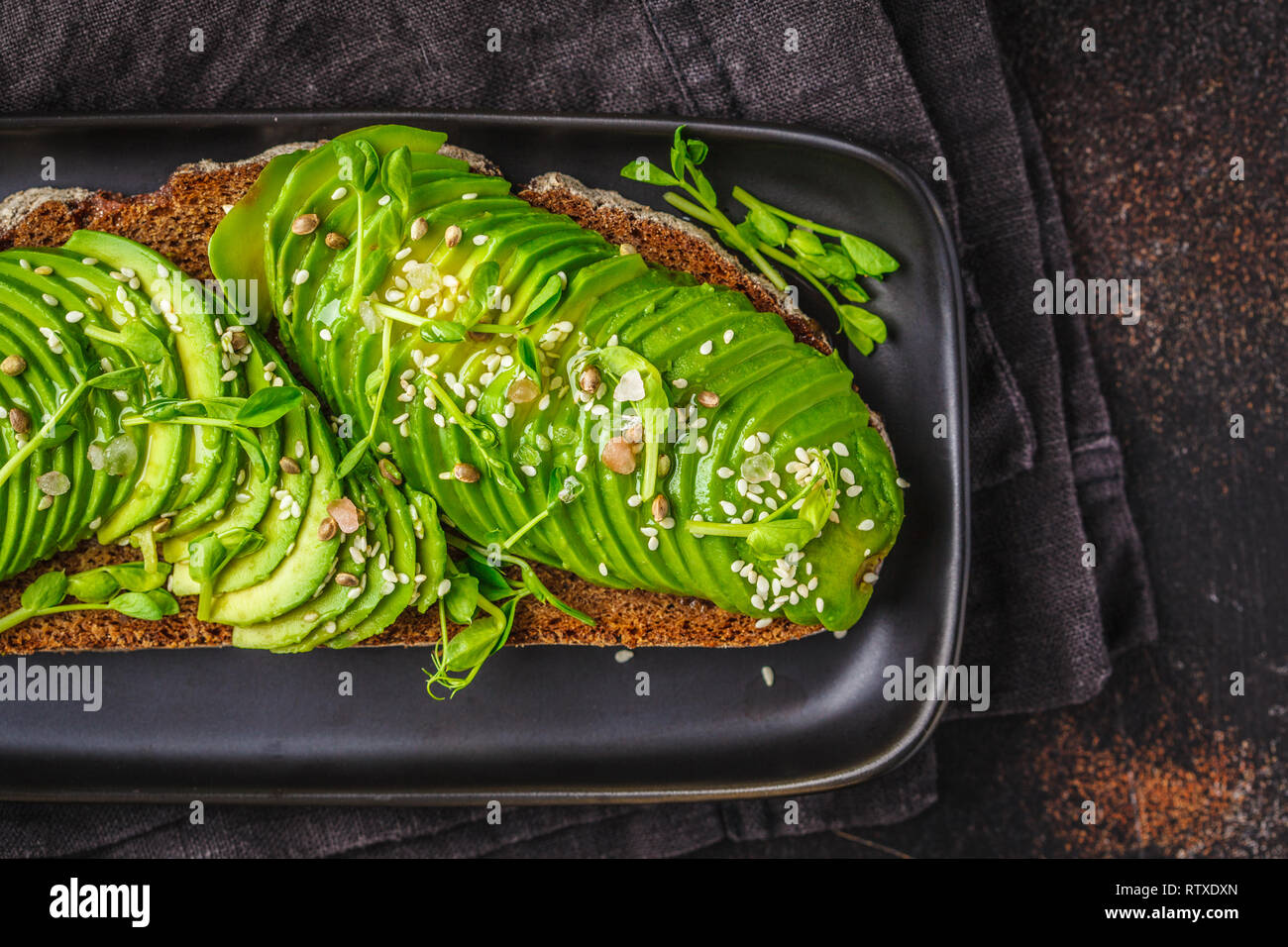 Avocado toast with rye bread and seeds on a black plate, dark ...