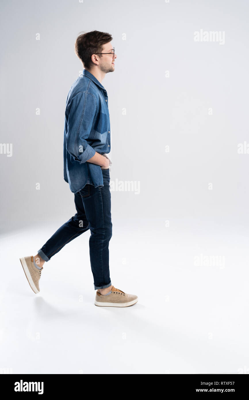 side view of a smiling young casual man walking, on white background ...