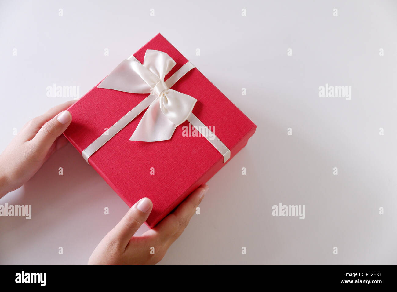 Close-up women hands sending red gift box with white ribbon on white ...