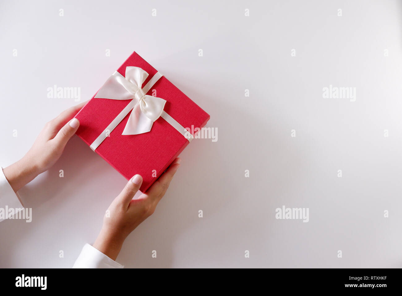 Close-up women hands sending red gift box with white ribbon on white ...