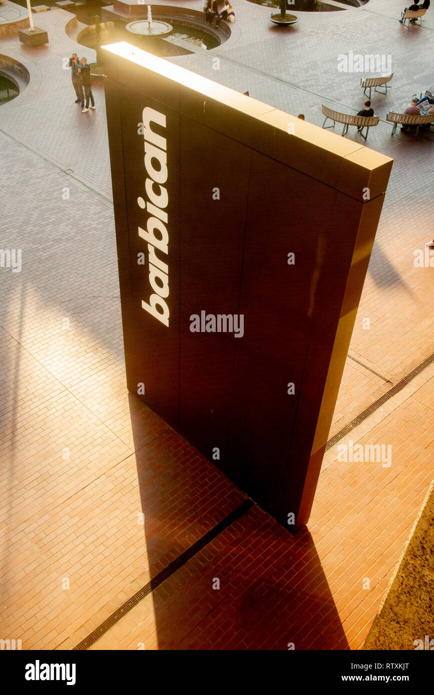 A large Barbican sign with people walking past with long shadows from ...