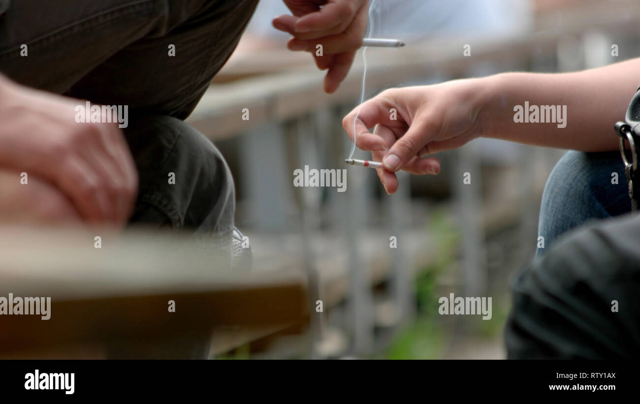 Young people holding burning cigarettes. Faceless female smoker with ...