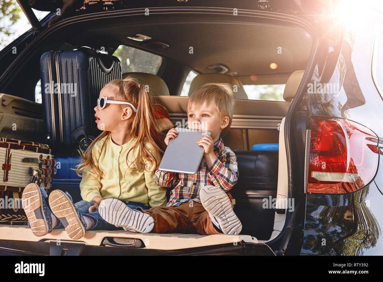 Two adorable caucasian kids sitting in a car trunk before going on ...
