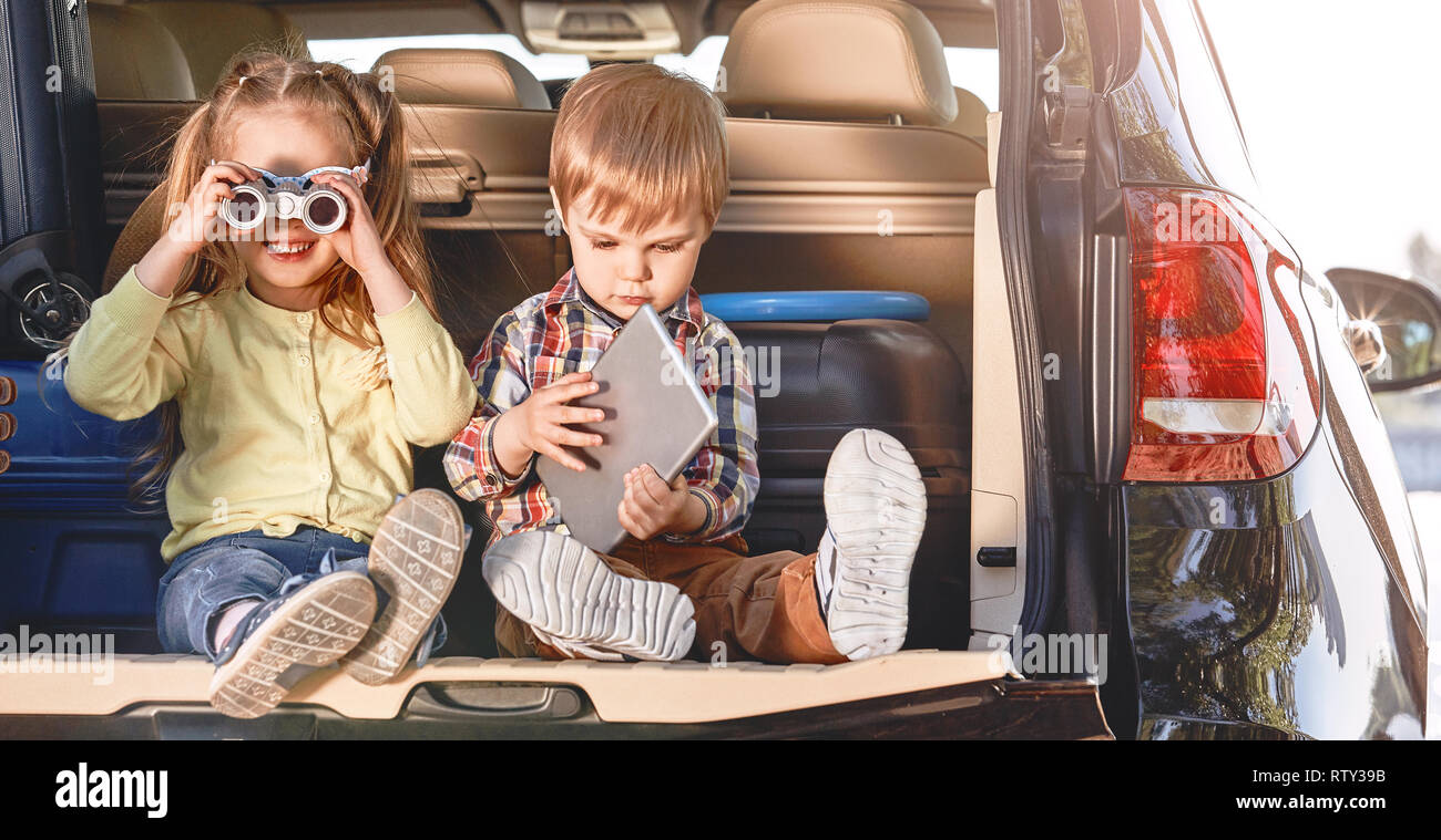 Two adorable caucasian kids sitting in a car trunk before going on ...