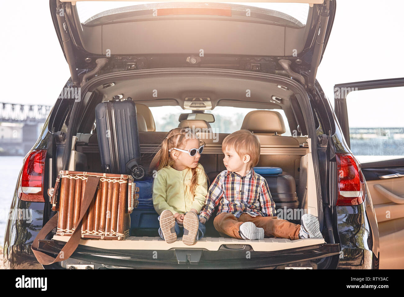 Two adorable caucasian kids sitting in a car trunk before going on ...