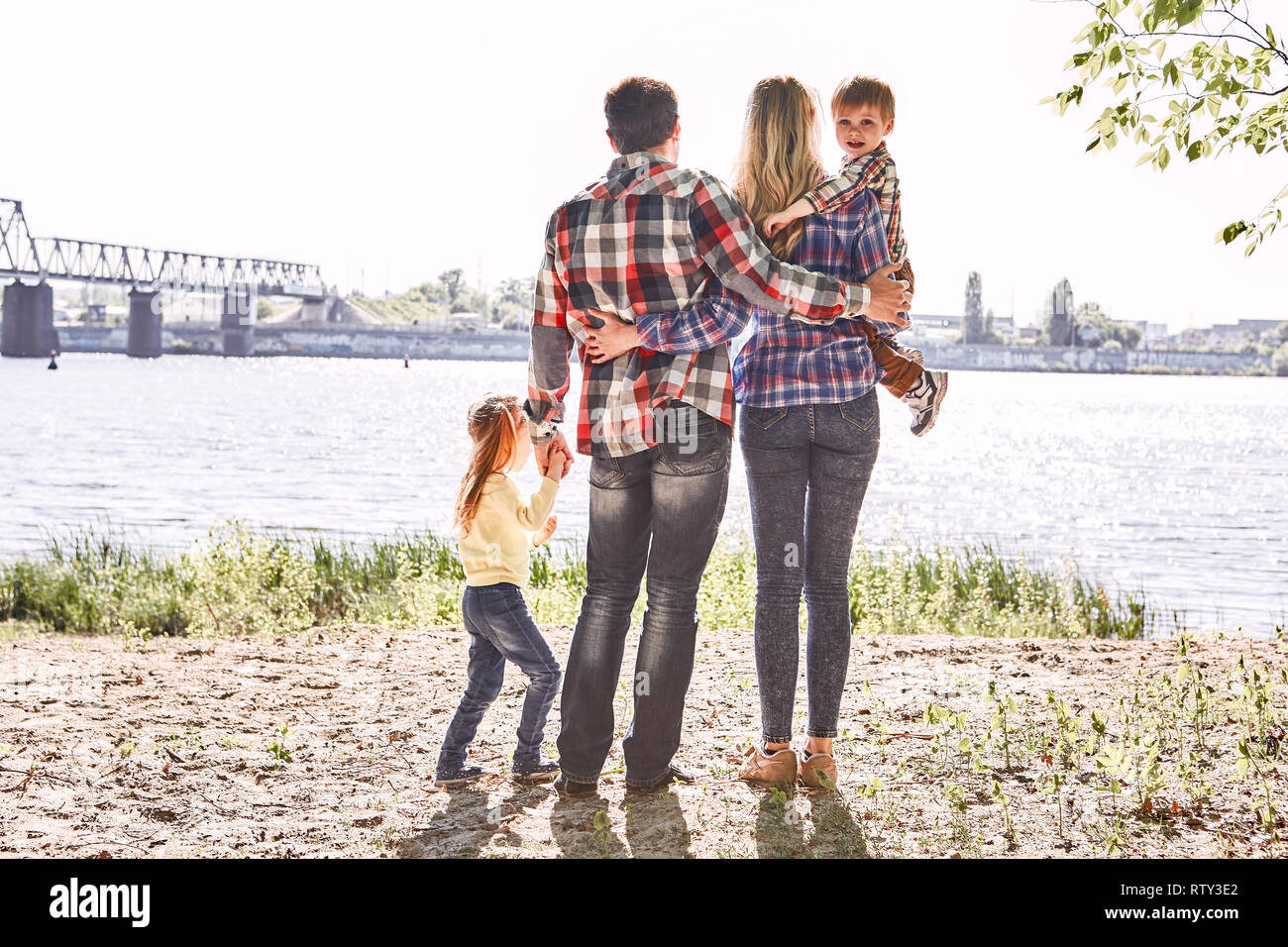 Young family of four holding hands. They are looking at summer landscape. Full length portrait ...
