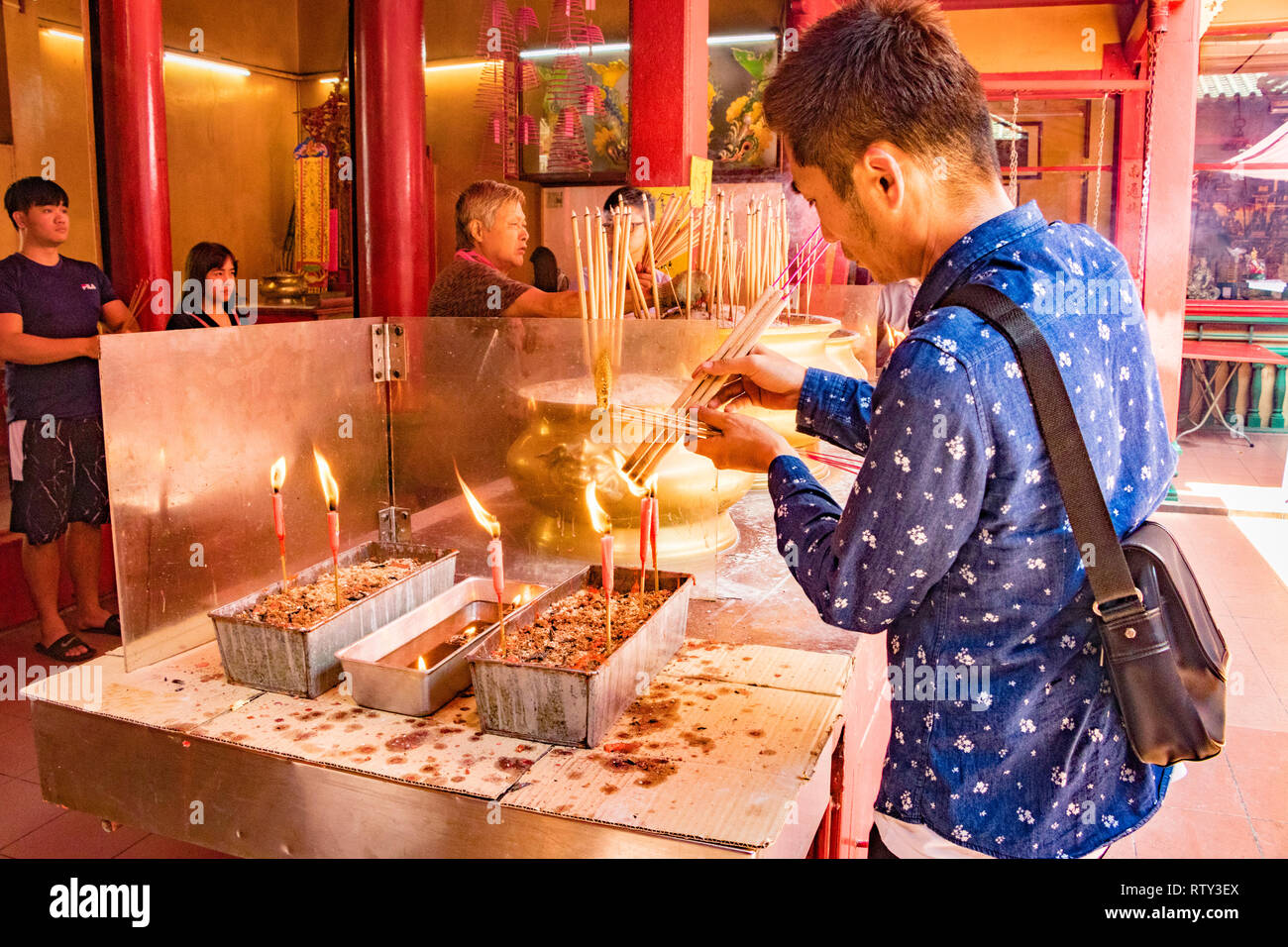 asian man lighting incense sticks in interior of Guan Di traditional ...