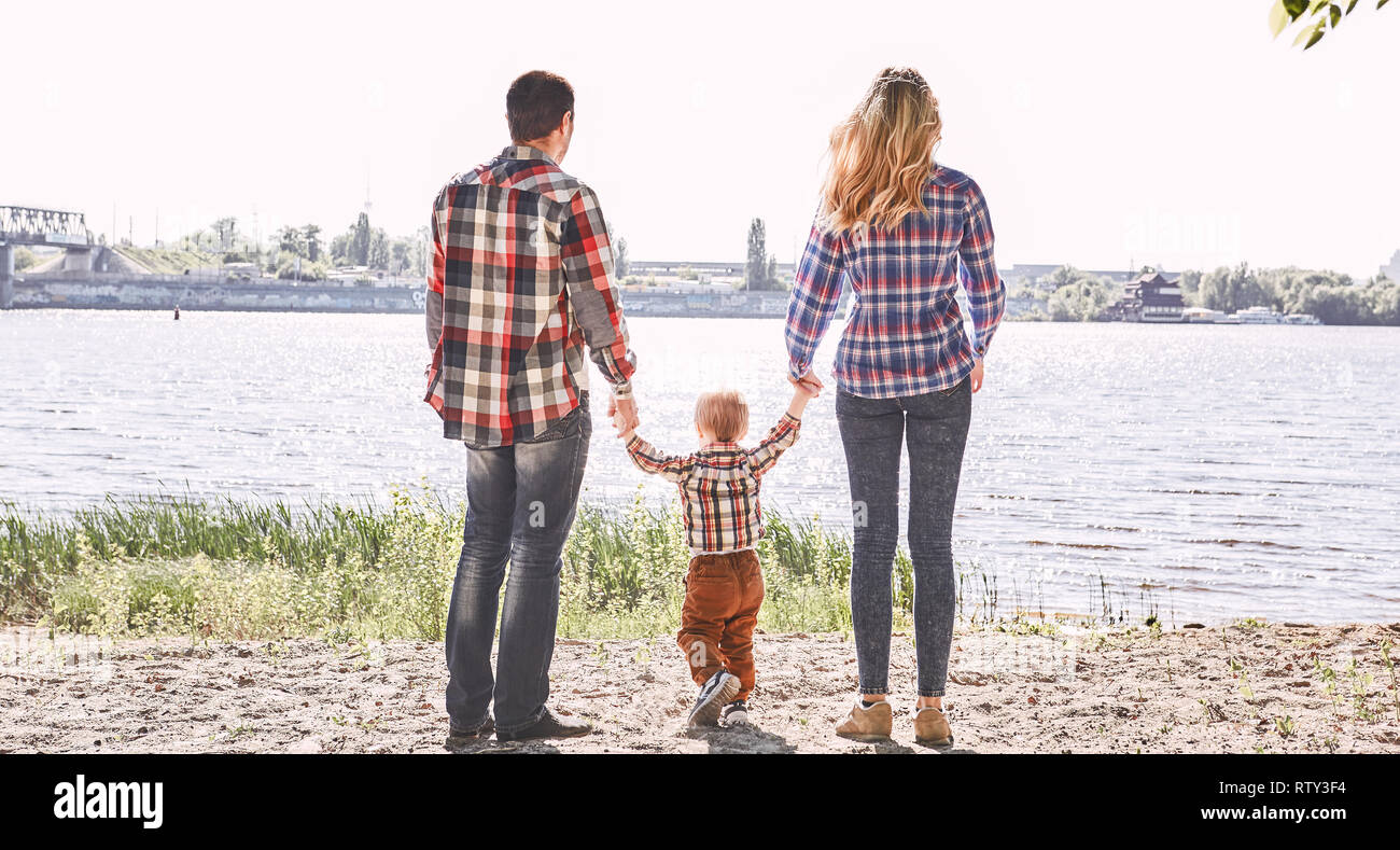 Sweet little kid standing in between his parents and holding their ...