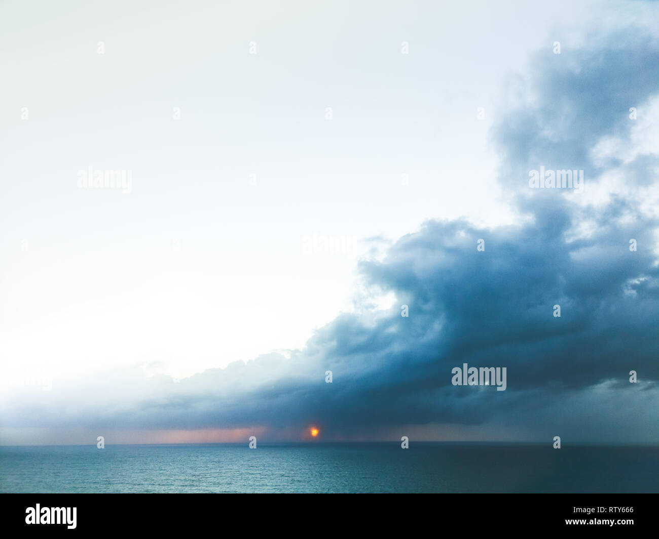 Storm clouds tower over the rising sun, as distant rain falls onto the ...