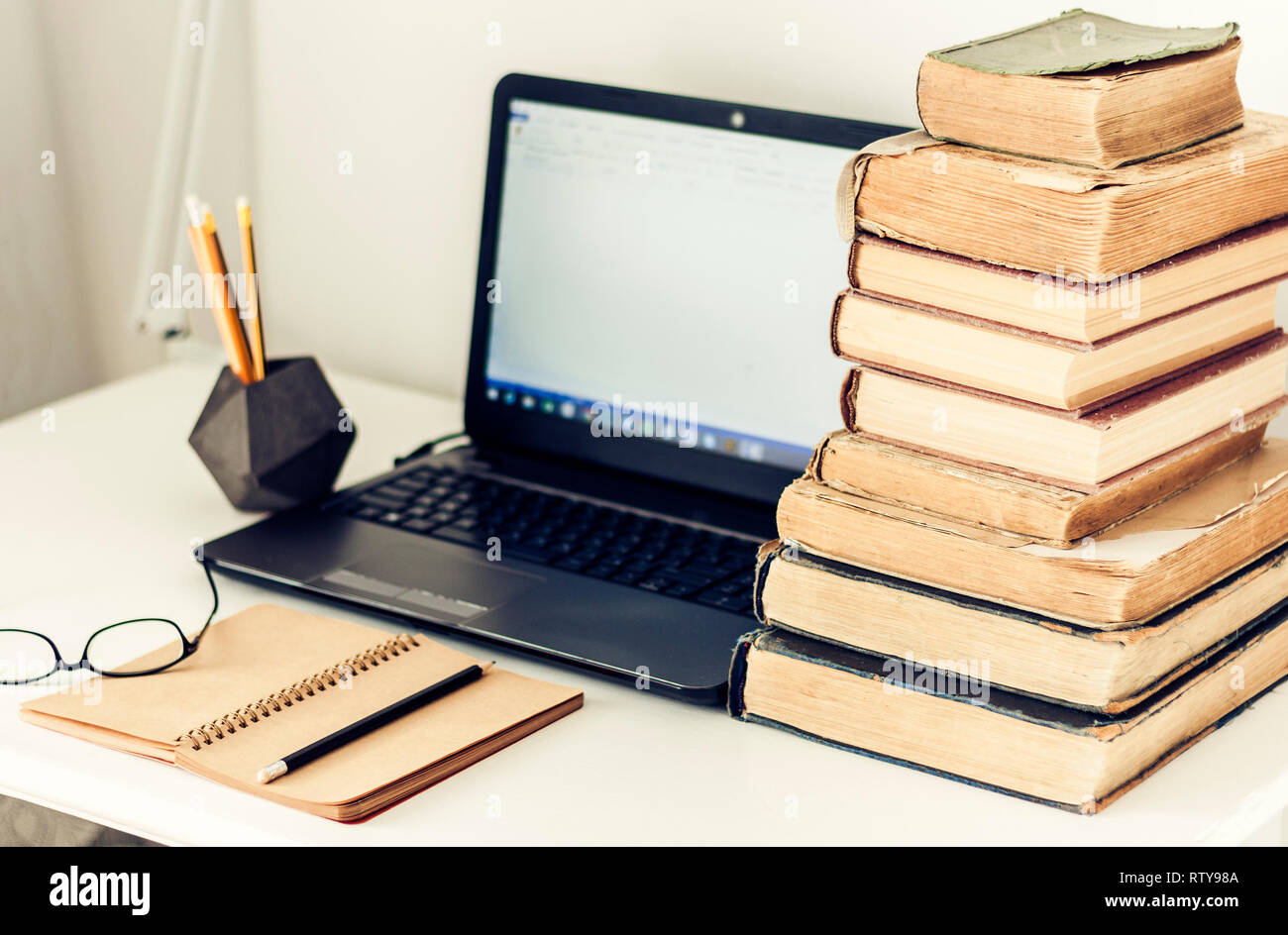 Laptop, stack of old books, notebook and pencils on white table ...