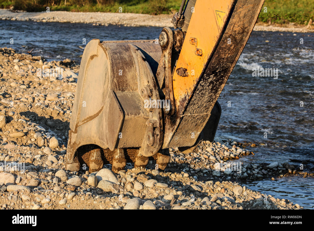 Digger (excavator machine) bucket digging stones ground by the river ...