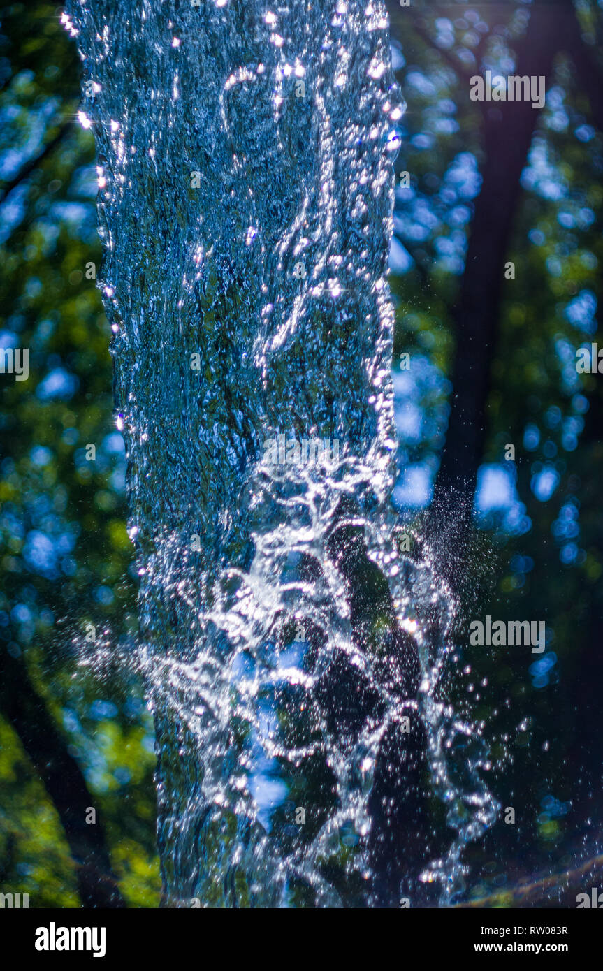 transparent falling water vertical flows against a blue sky and green ...