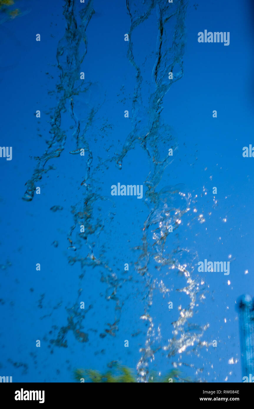 transparent falling water vertical flows against a blue sky and green ...