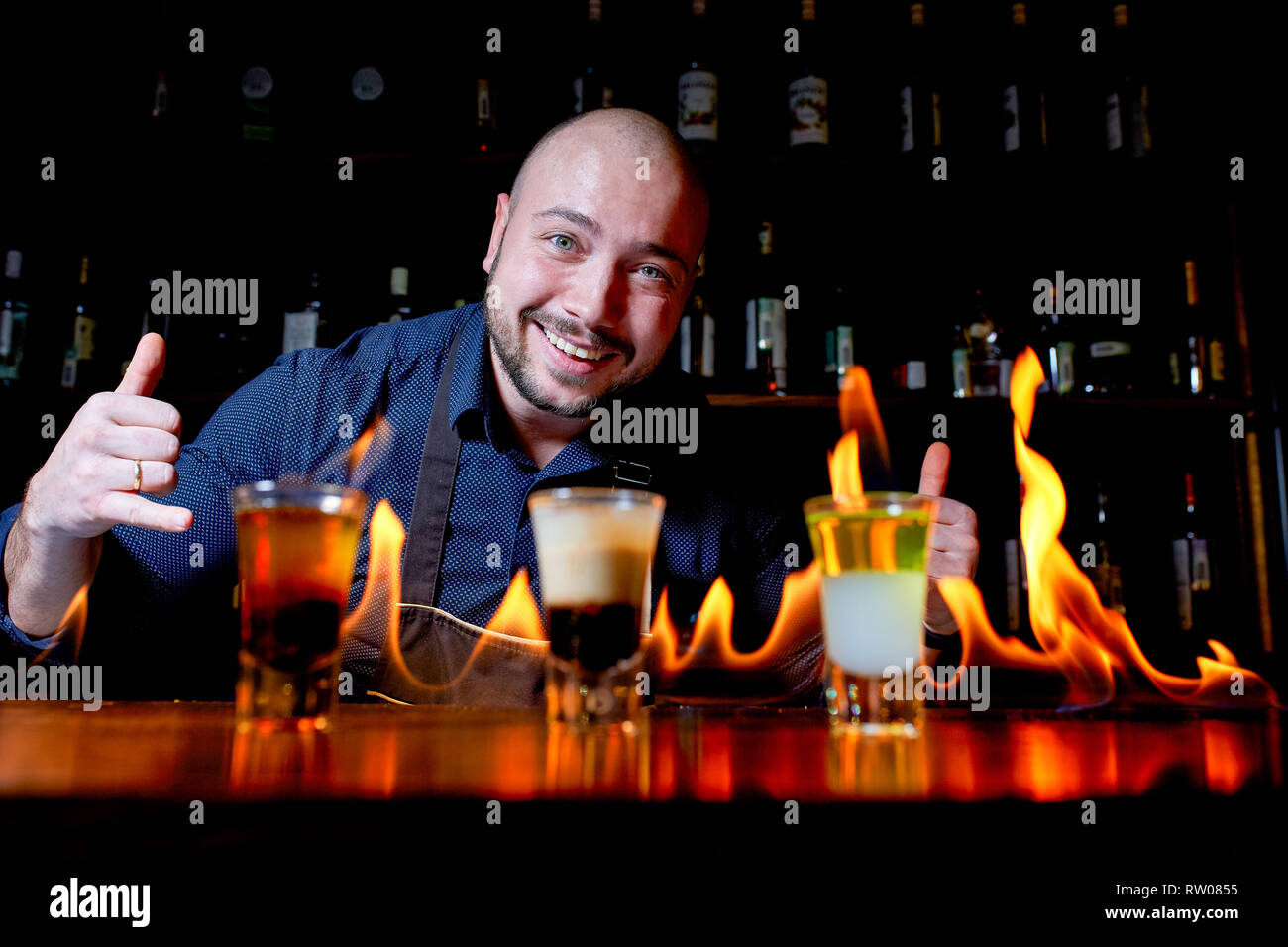 Fiery show at the bar. The bartender makes hot alcoholic cocktail and ...