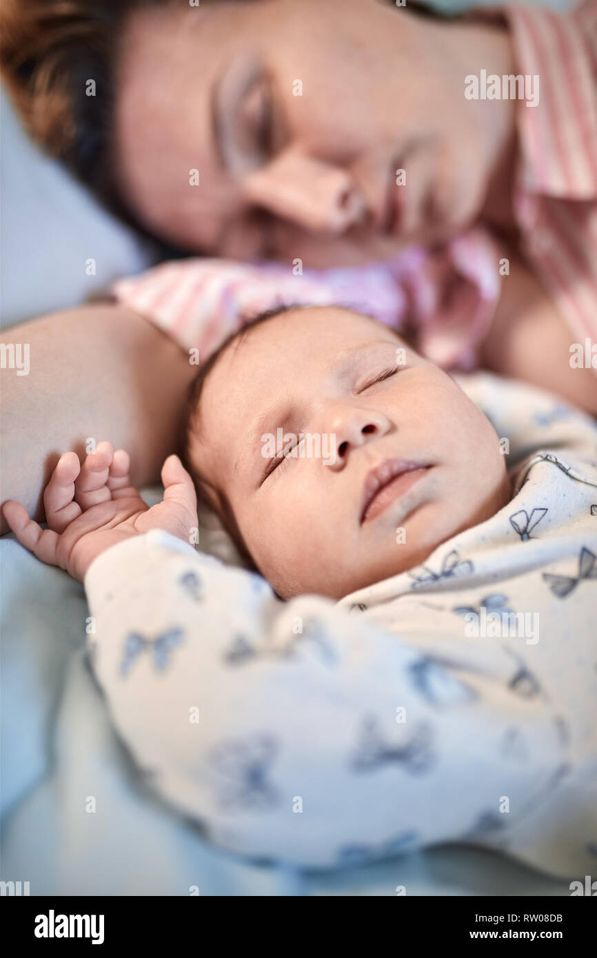 Portrait of newborn baby and mother sleeping on bed, resting together ...
