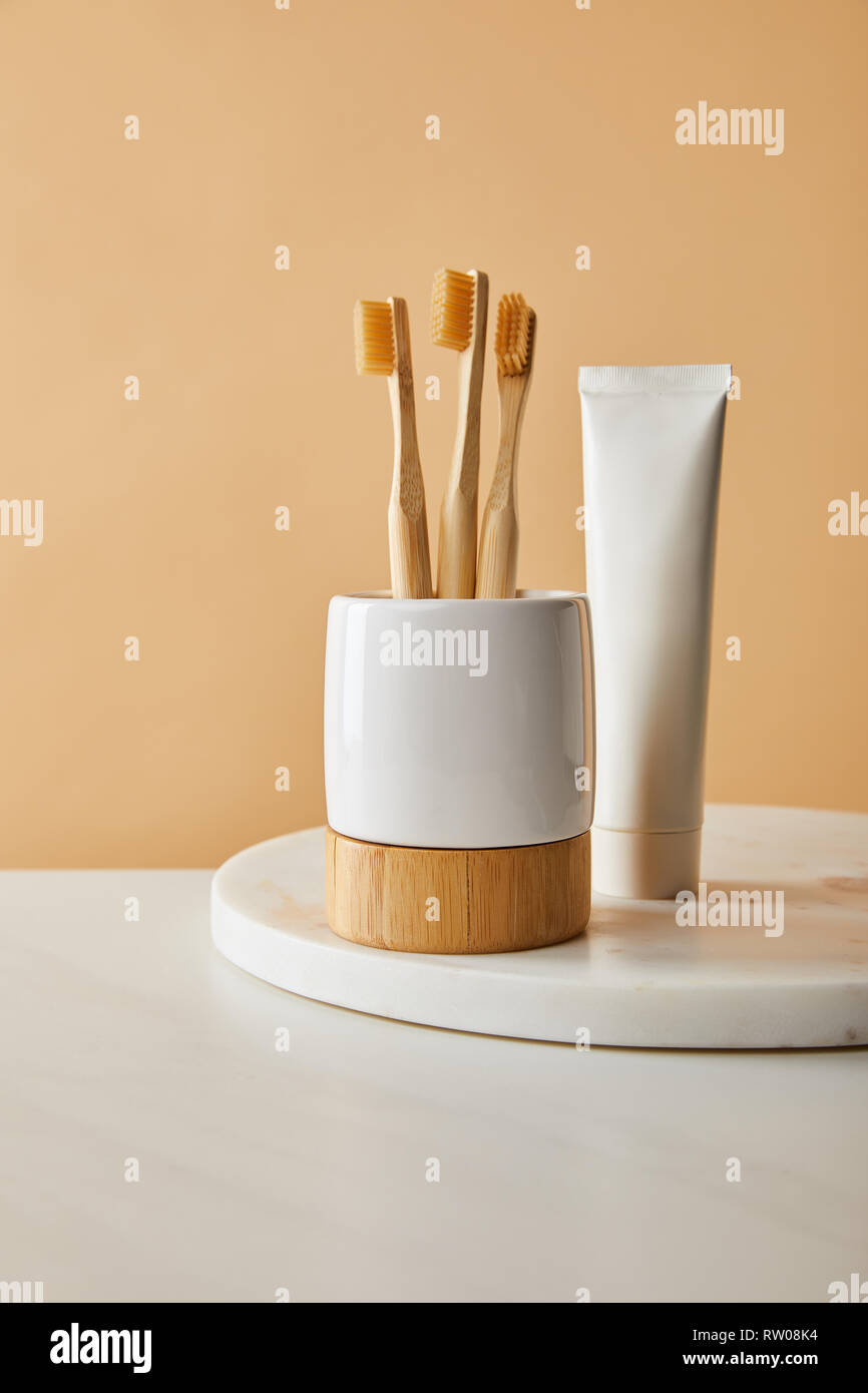 toothpaste in tube and holder with bamboo toothbrushes on white marble ...
