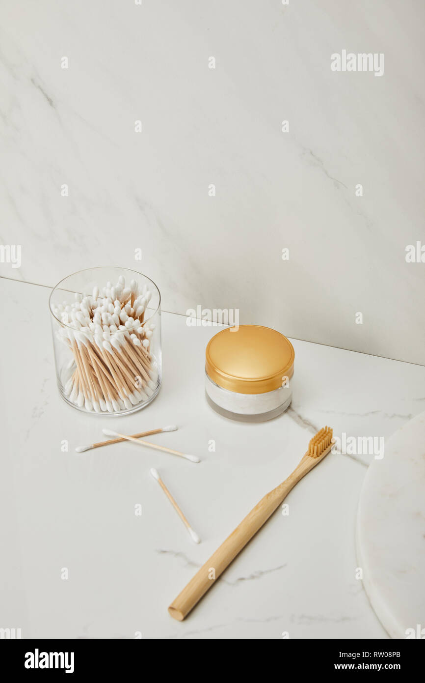 ear sticks in glass, cosmetic cream and bamboo toothbrush on white ...