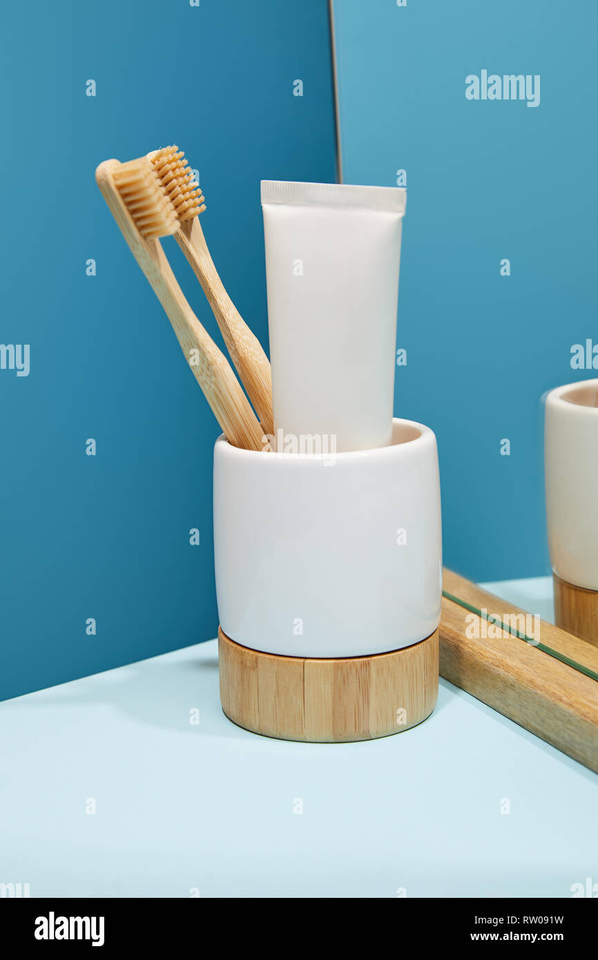 holder with bamboo toothbrushes, toothpaste in tube and mirror on table ...