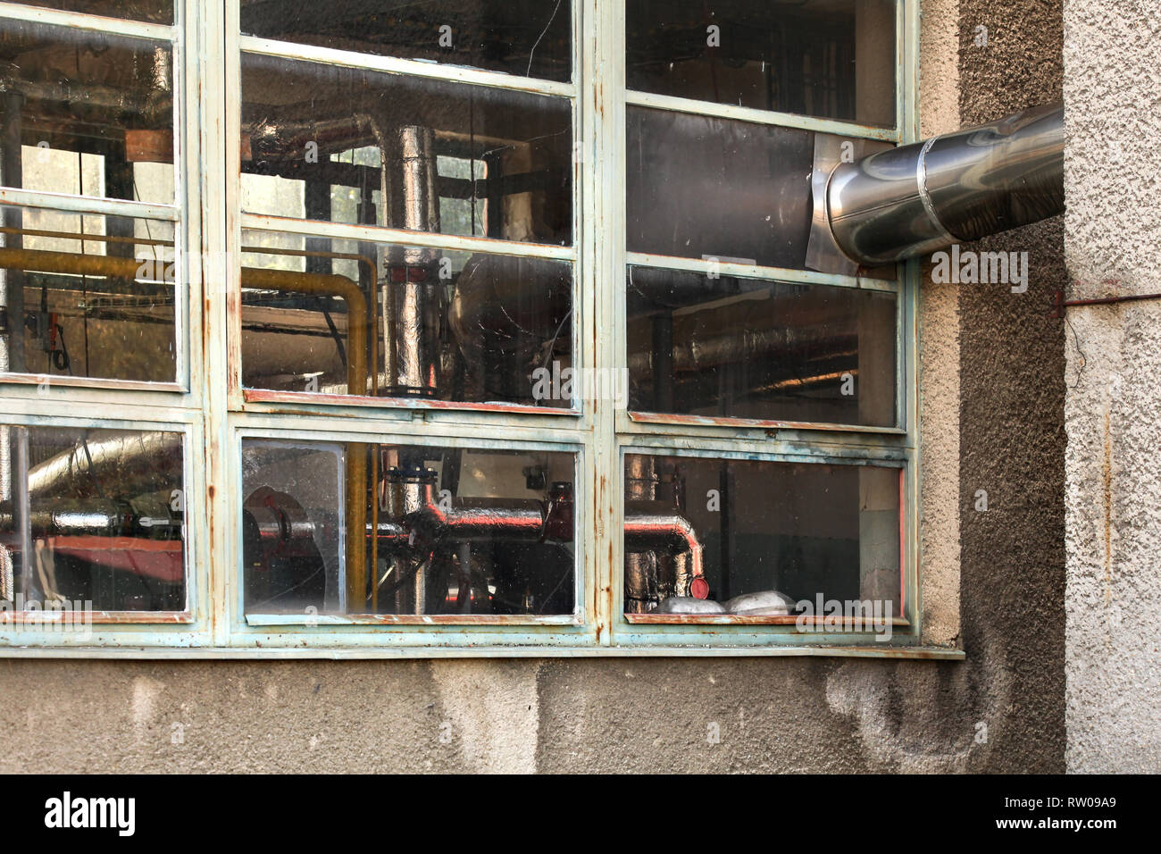 Small old heating plant windows from outside. Heat pipes covered in ...