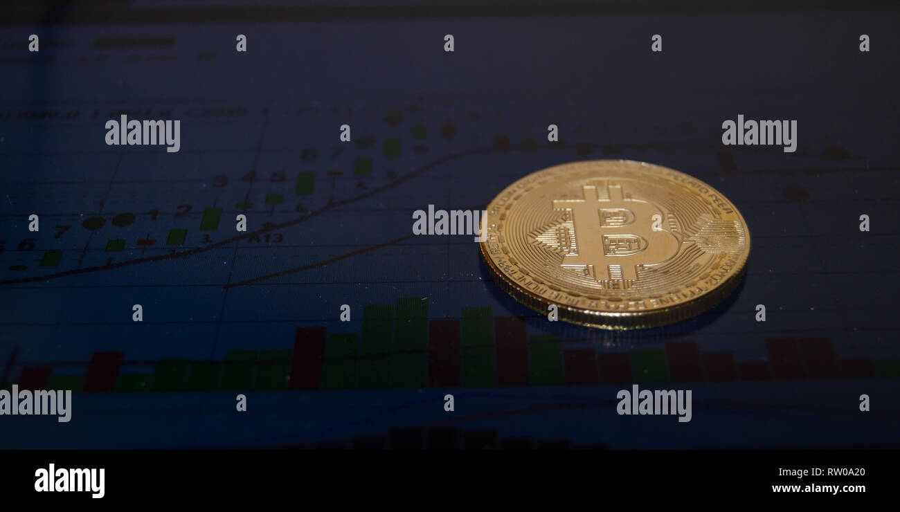 close up of one bitcoin over the monitor showing stock market chart ...