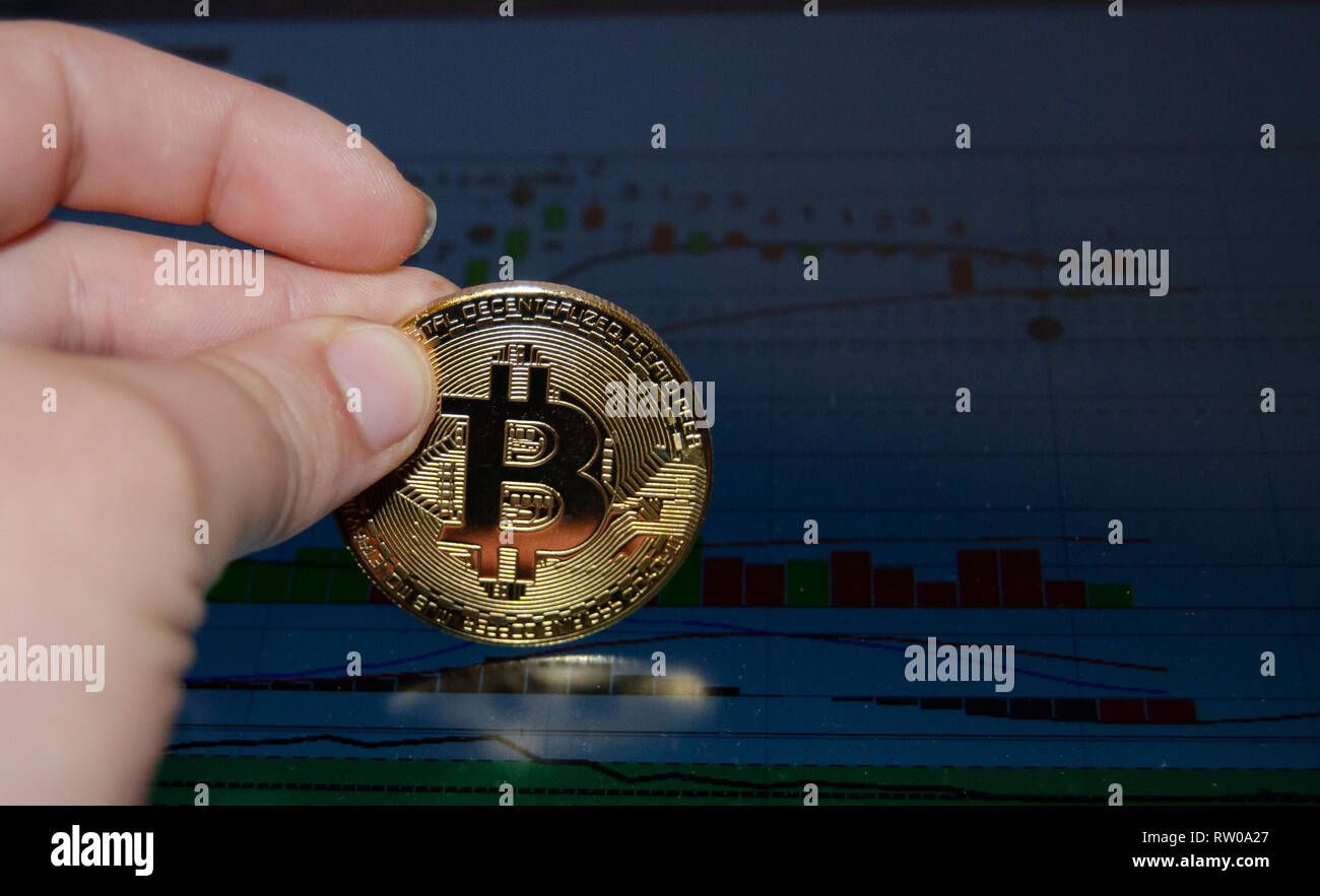 close up of one bitcoin over the monitor showing stock market chart ...