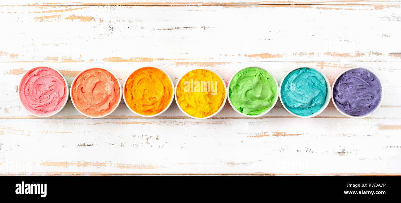 Many cups with colorful rainbow ice cream placed in a row on white ...