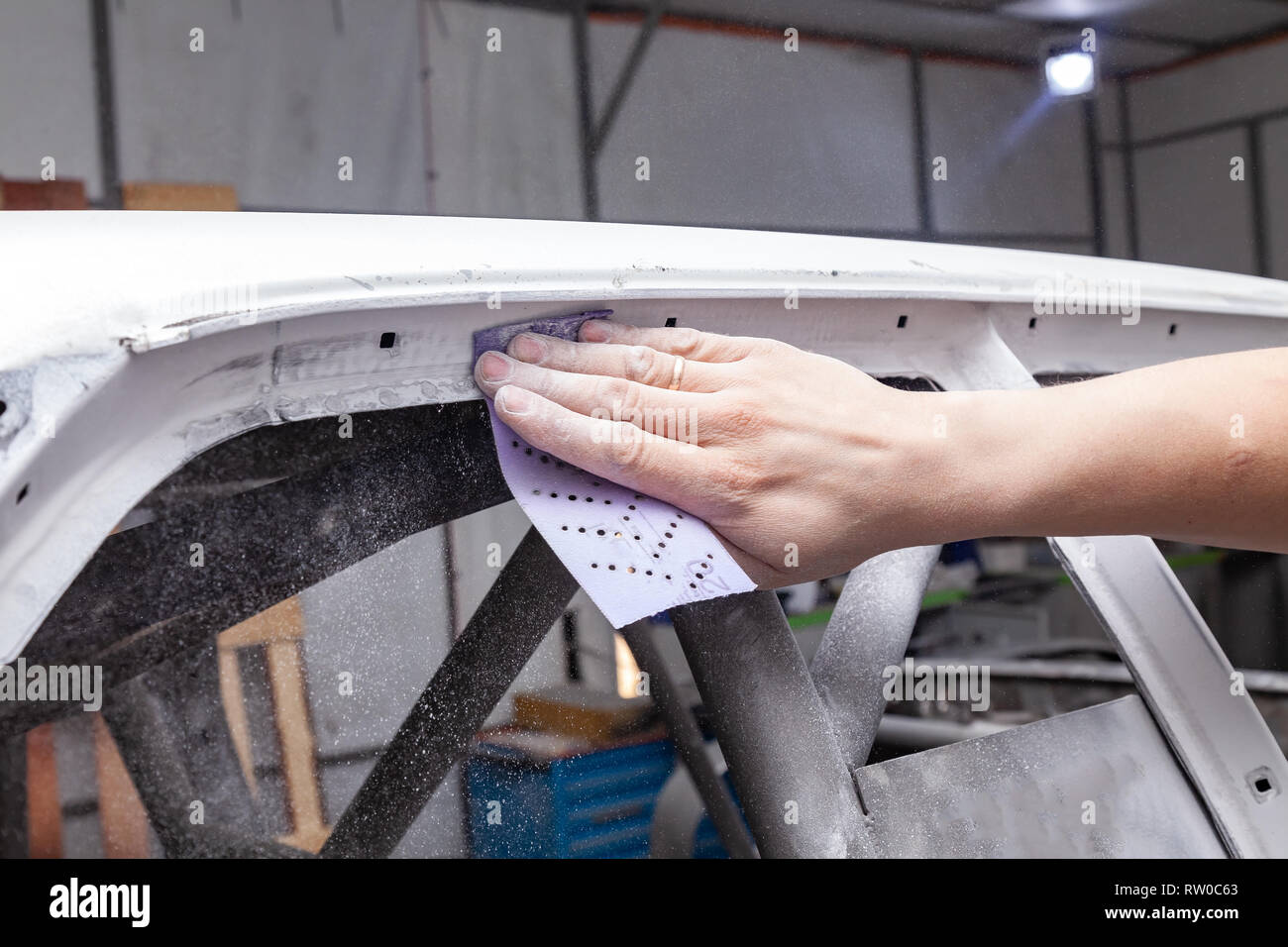 The body repairman grinds the white car's frame with purple emery paper ...