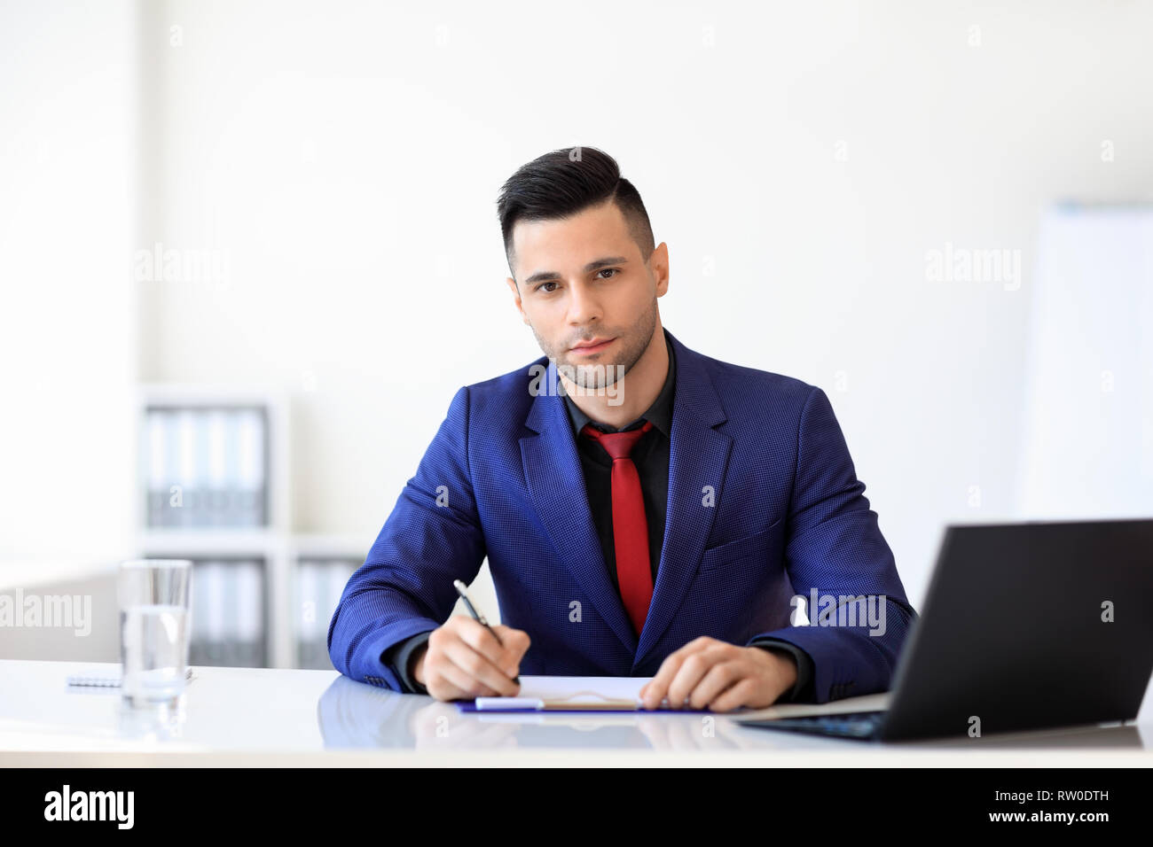 Portrait of young confident businessman signing document sitting at his ...