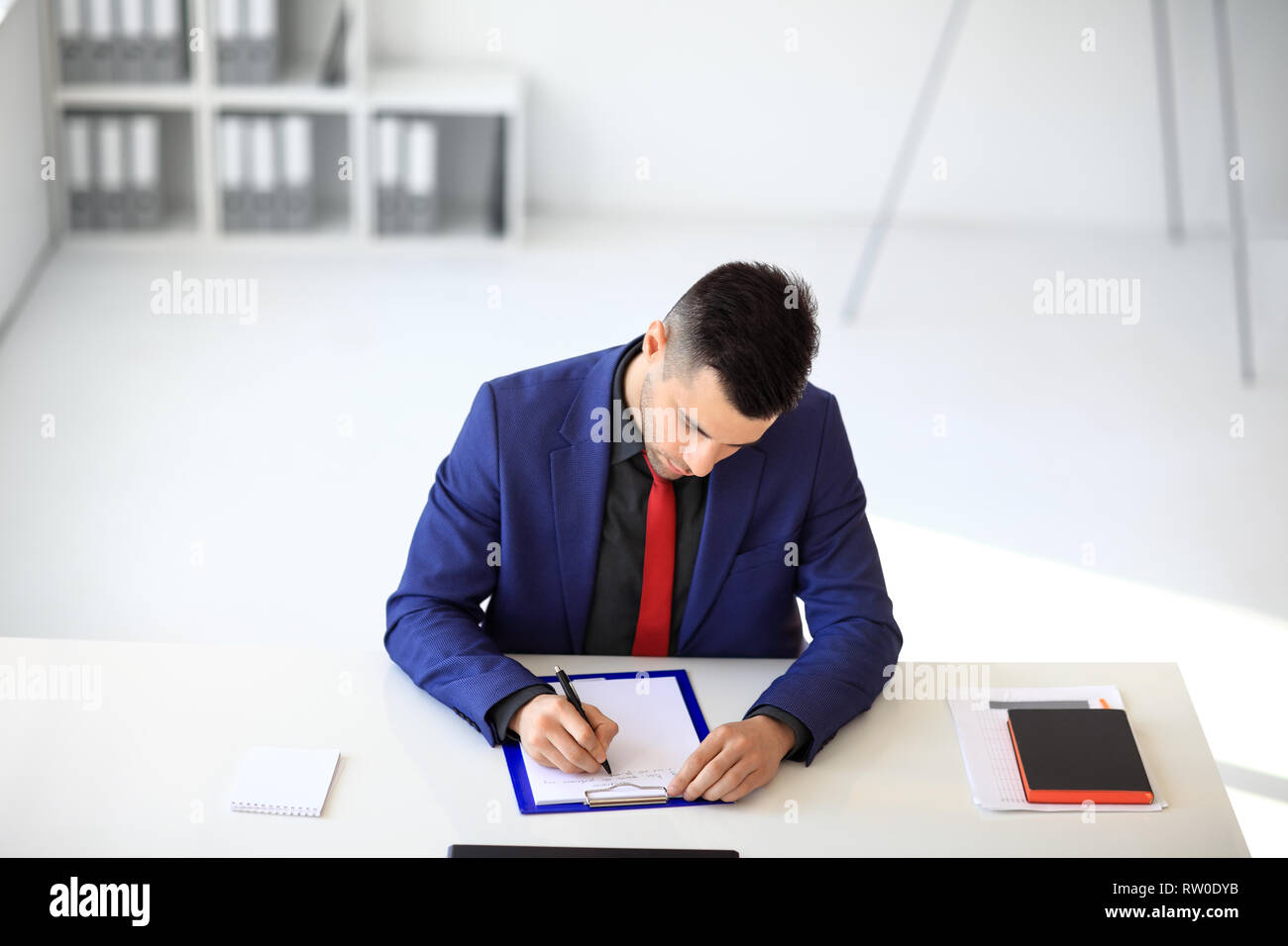 Portrait of young confident businessman signing document sitting at his ...