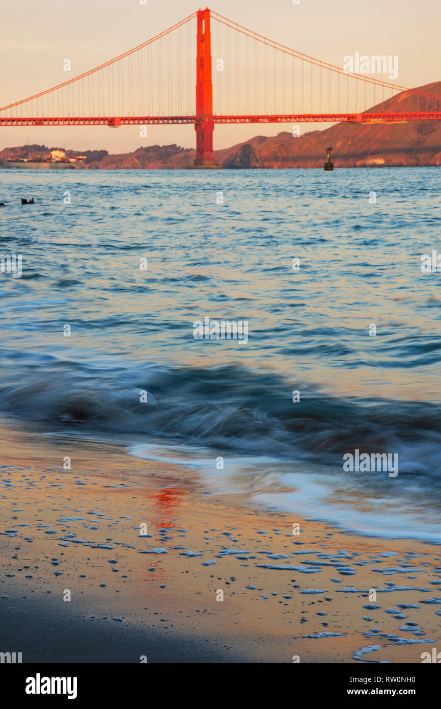 Golden Gate Bridge in warm red color of aurora and it’s reflection on ...