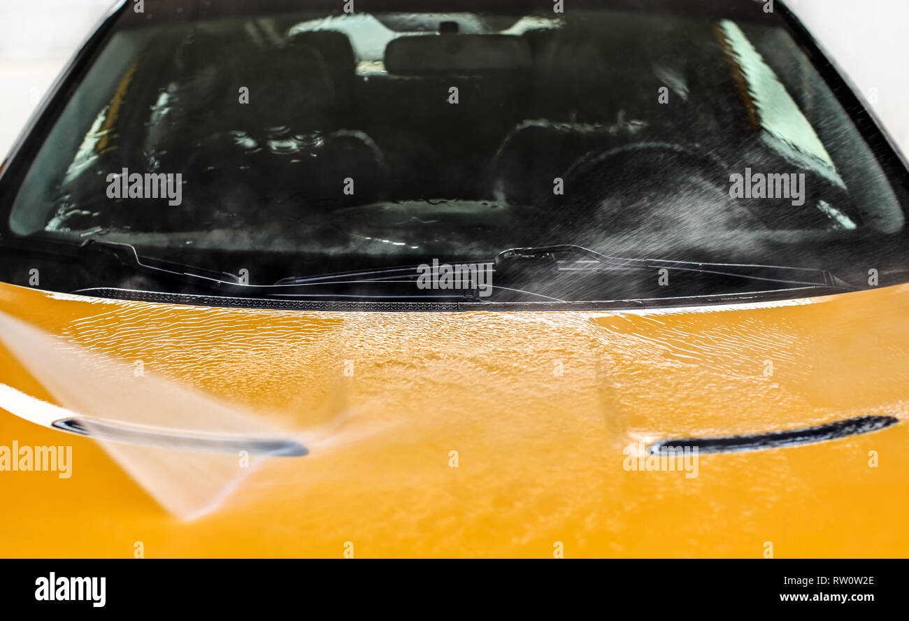 Water jet spraying on front of yellow car washed in self serve carwash ...