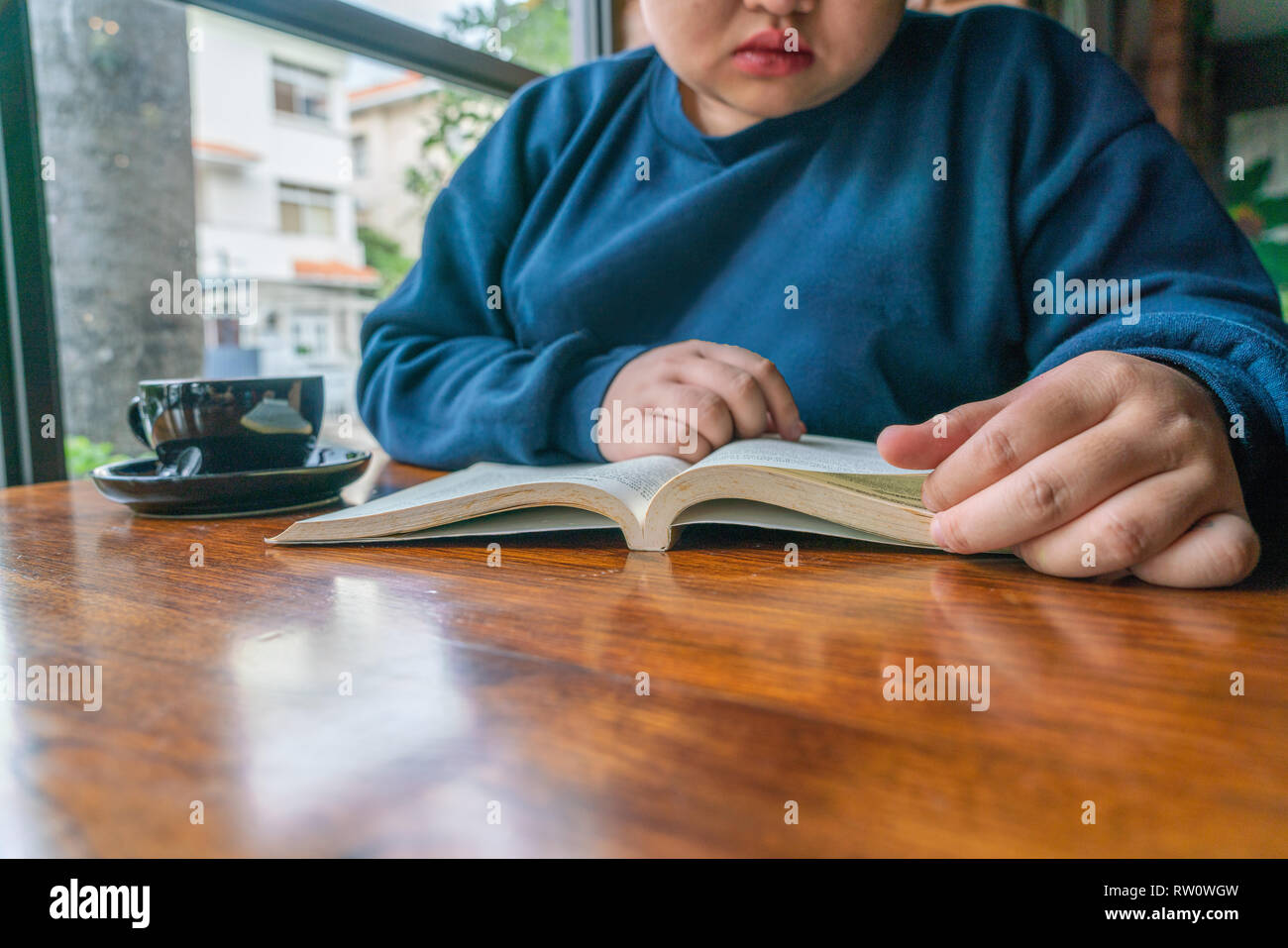 Young girl sitting by wooden table and reading book Stock Photo - Alamy