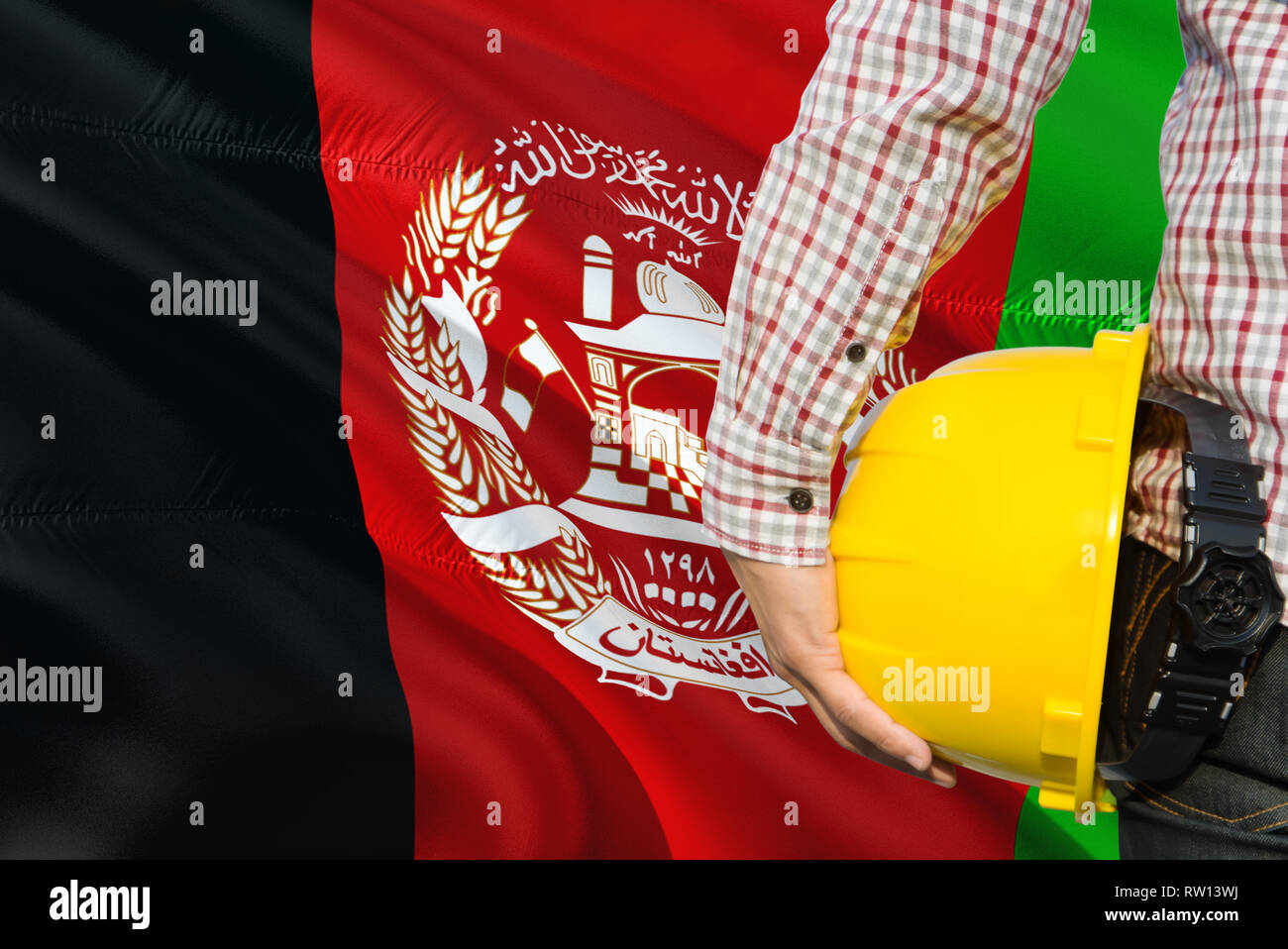 Afghan Engineer is holding yellow safety helmet with waving Afghanistan flag background ...