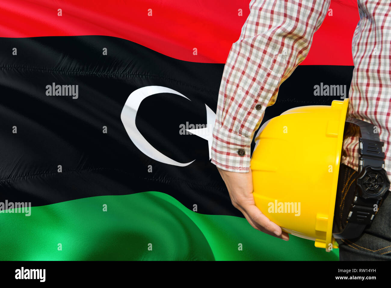 Libyan Engineer is holding yellow safety helmet with waving Libya flag ...