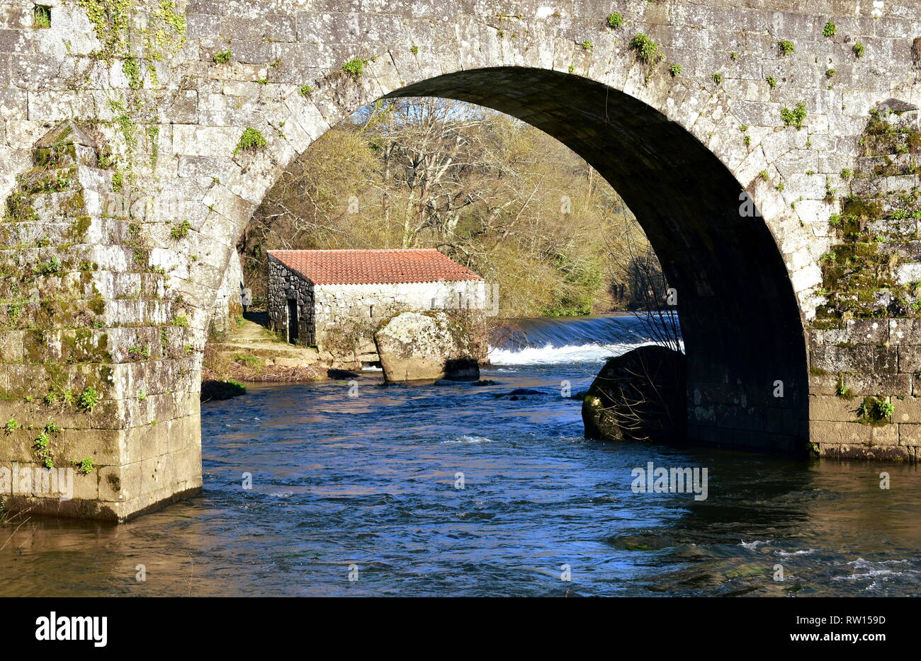 River with old stone water mill and waterfall under an ancient bridge ...