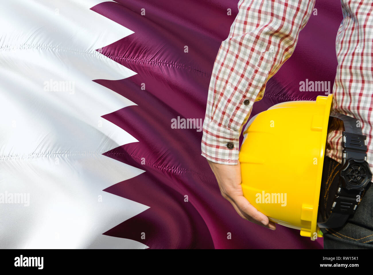 Qatari Engineer is holding yellow safety helmet with waving Qatar flag ...