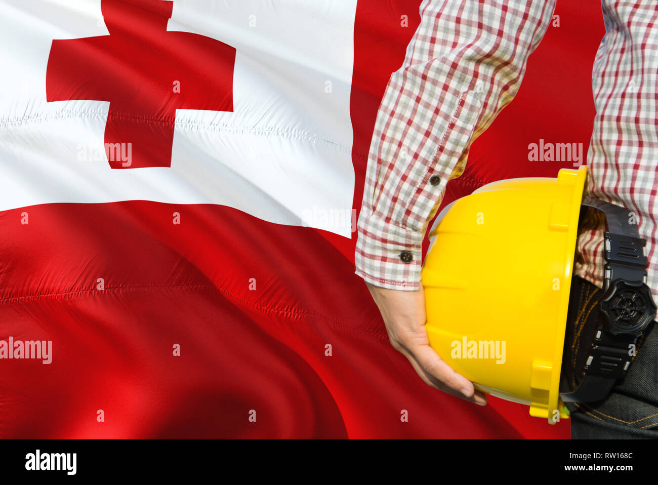 Tongan Engineer is holding yellow safety helmet with waving Tonga flag ...