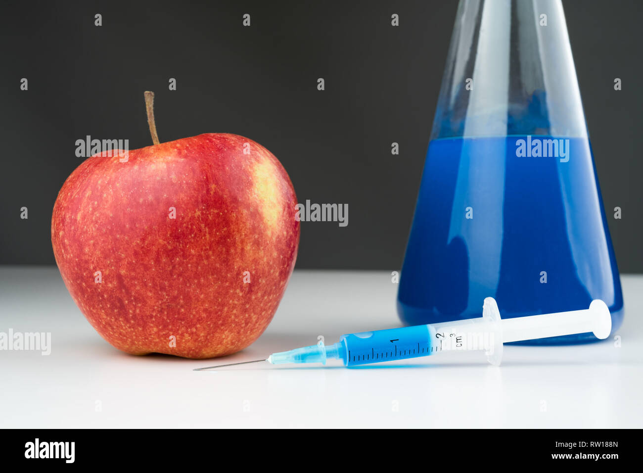 Blue liquid, apple and syringe on a white laboratory table. Genetically ...