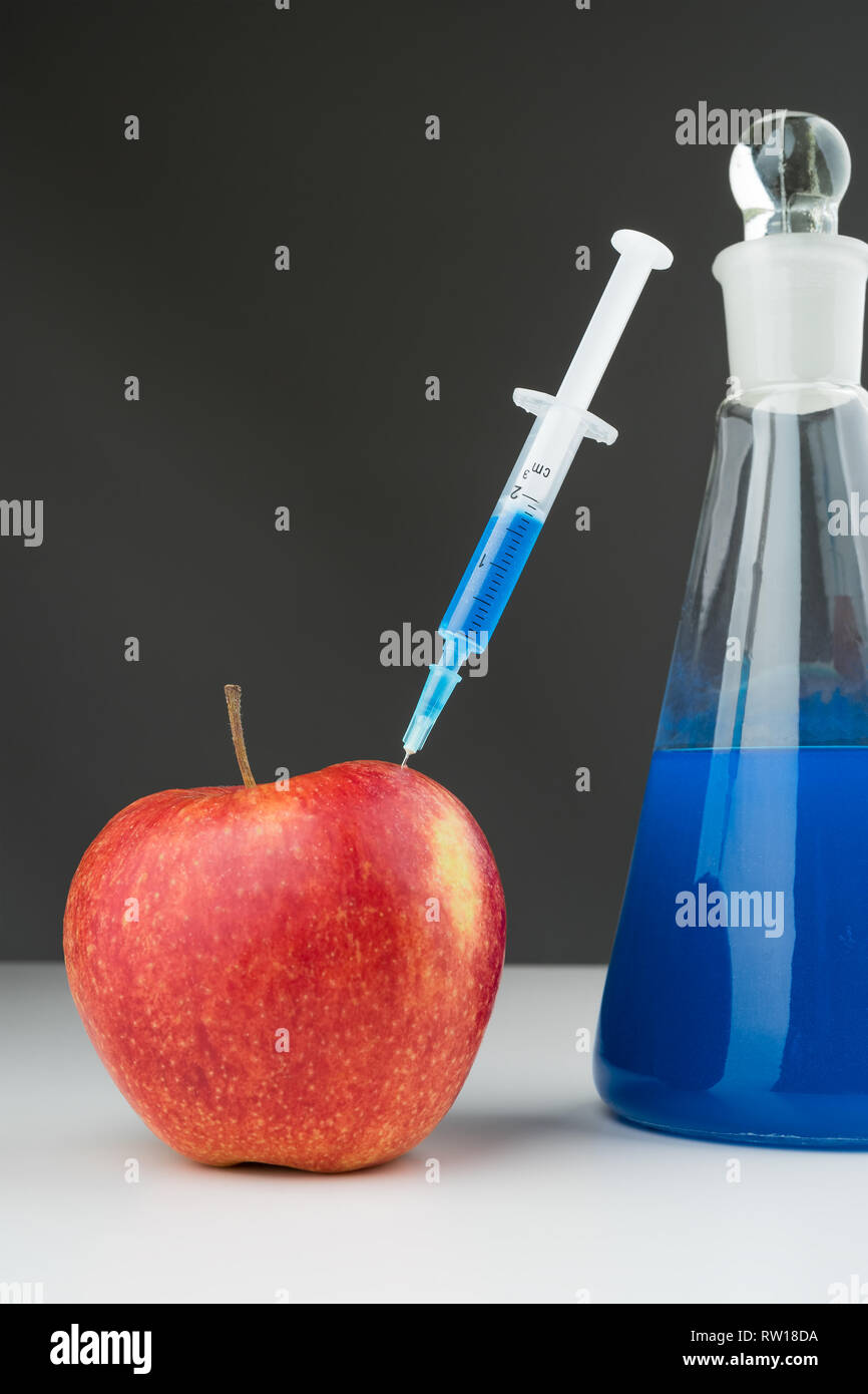 Blue liquid, apple and syringe on a white laboratory table. Genetically ...