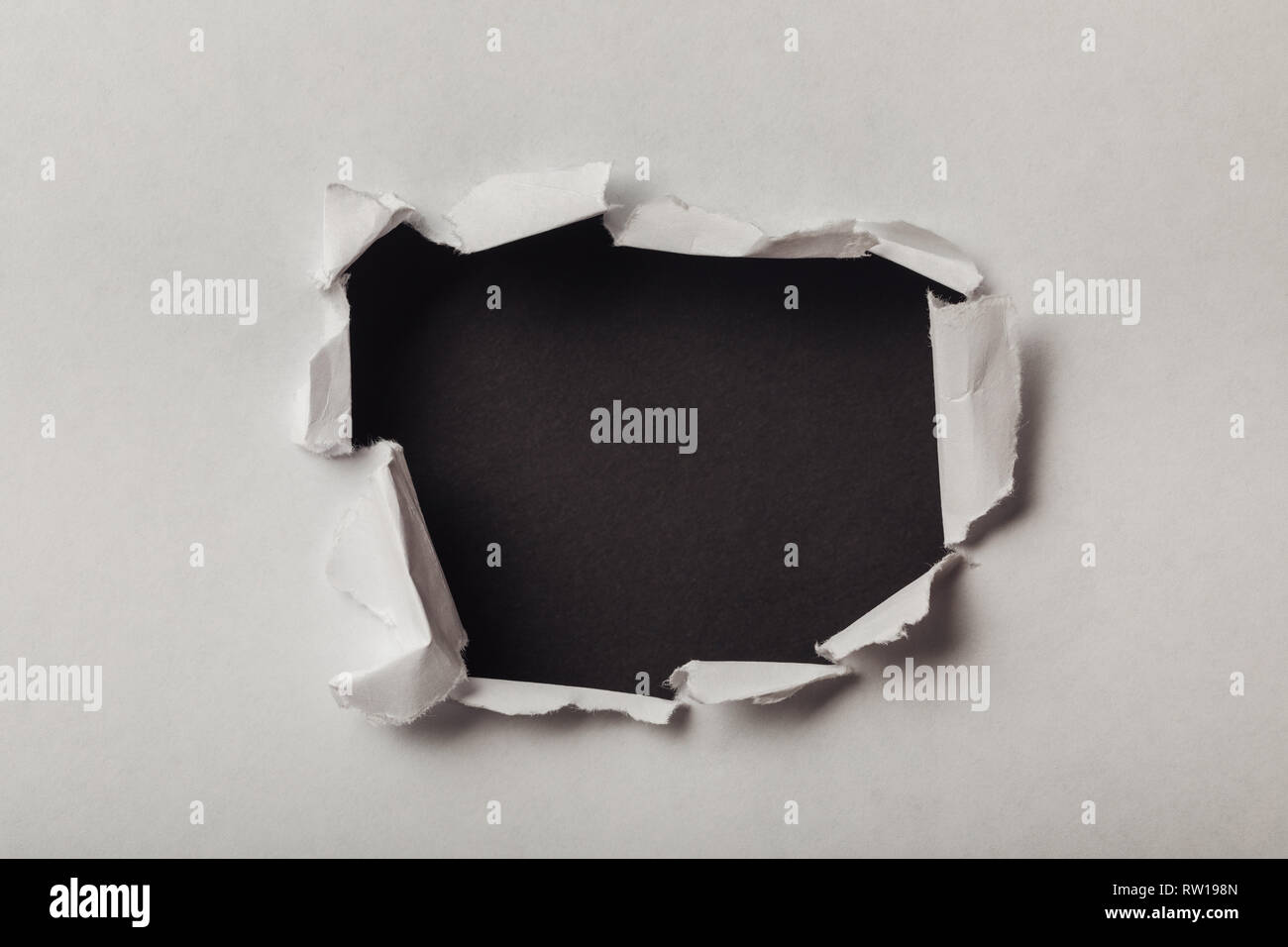 torn hole in sheet of paper on black background Stock Photo - Alamy