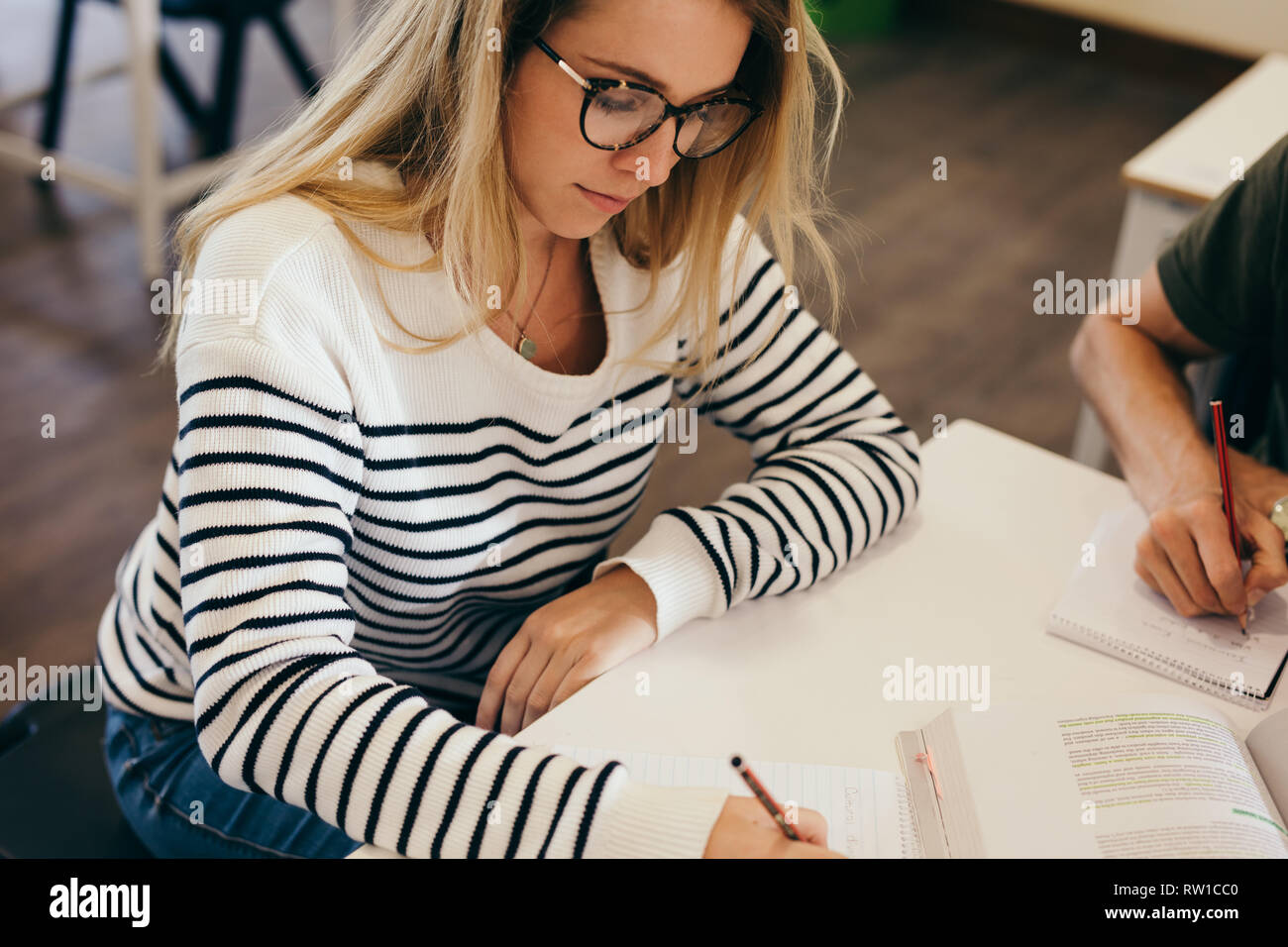 Girl writing in book with classmates sitting by. Female students ...