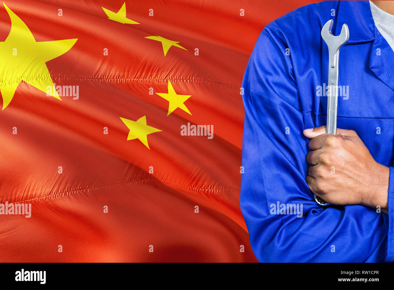 Chinese Mechanic in blue uniform is holding wrench against waving China ...
