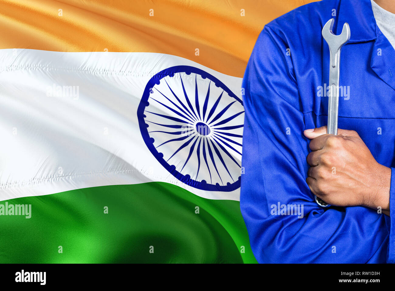 Indian Mechanic in blue uniform is holding wrench against waving India ...
