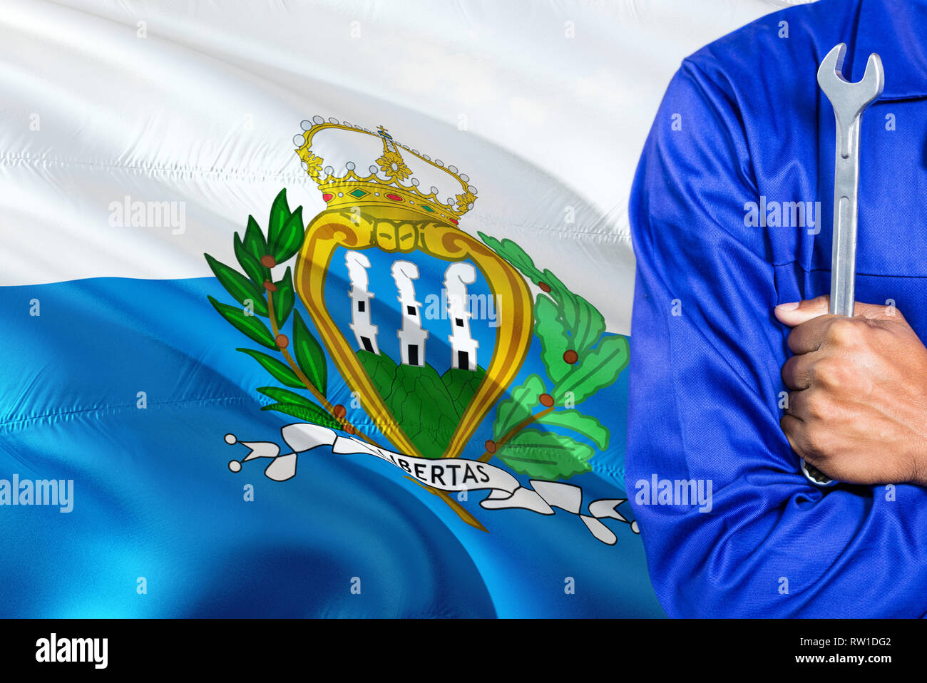 Sammarinese Mechanic in blue uniform is holding wrench against waving ...