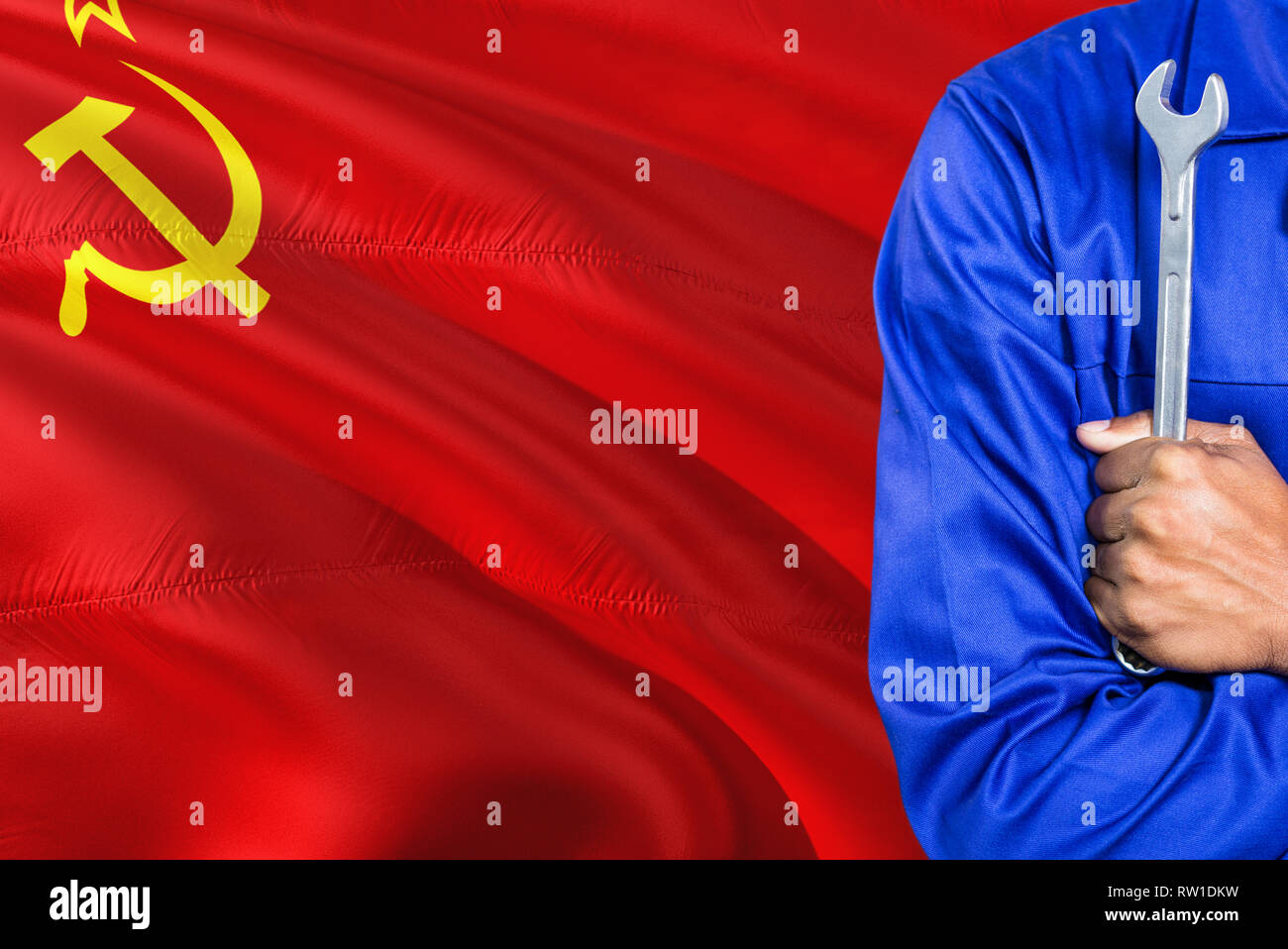 Mechanic in blue uniform is holding wrench against waving Soviet Union ...