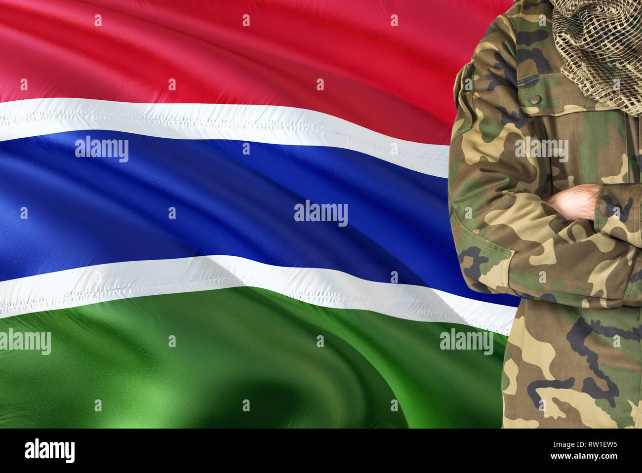 Crossed arms Gambian soldier with national waving flag on background ...