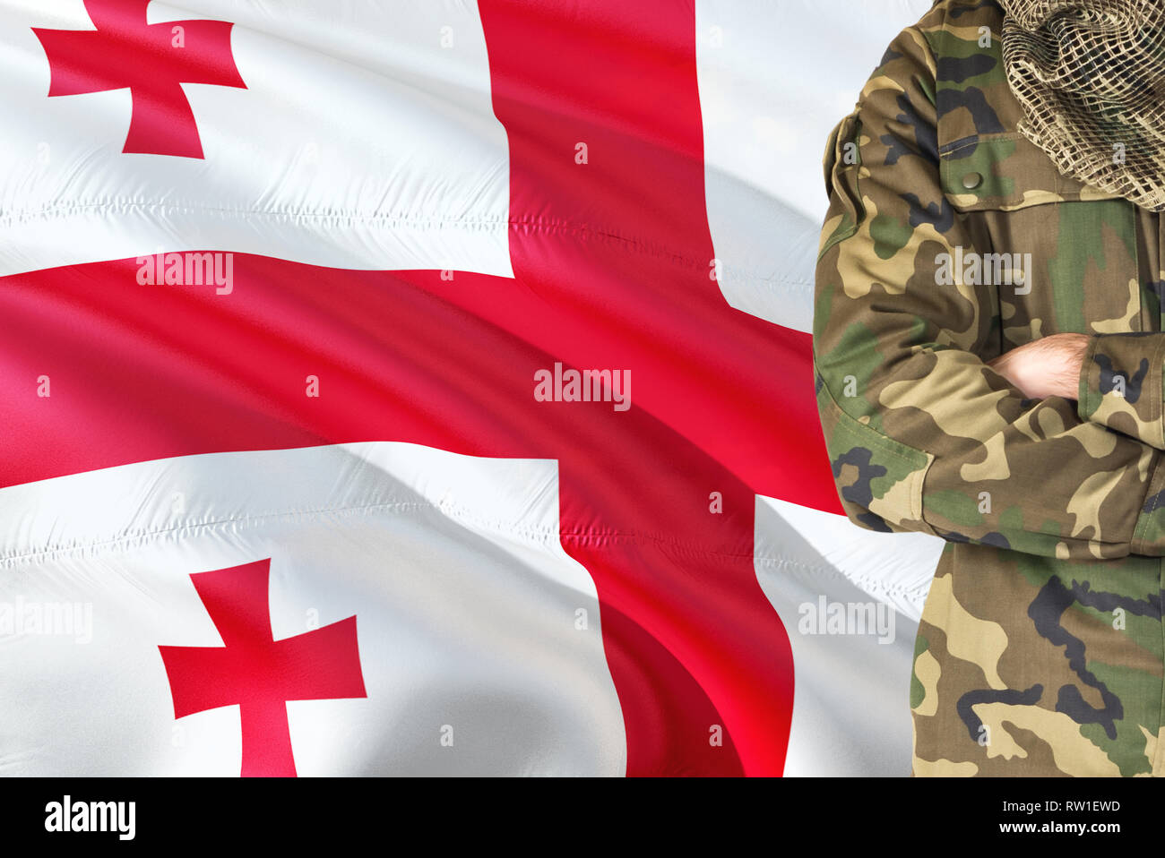 Crossed arms Georgian soldier with national waving flag on background ...