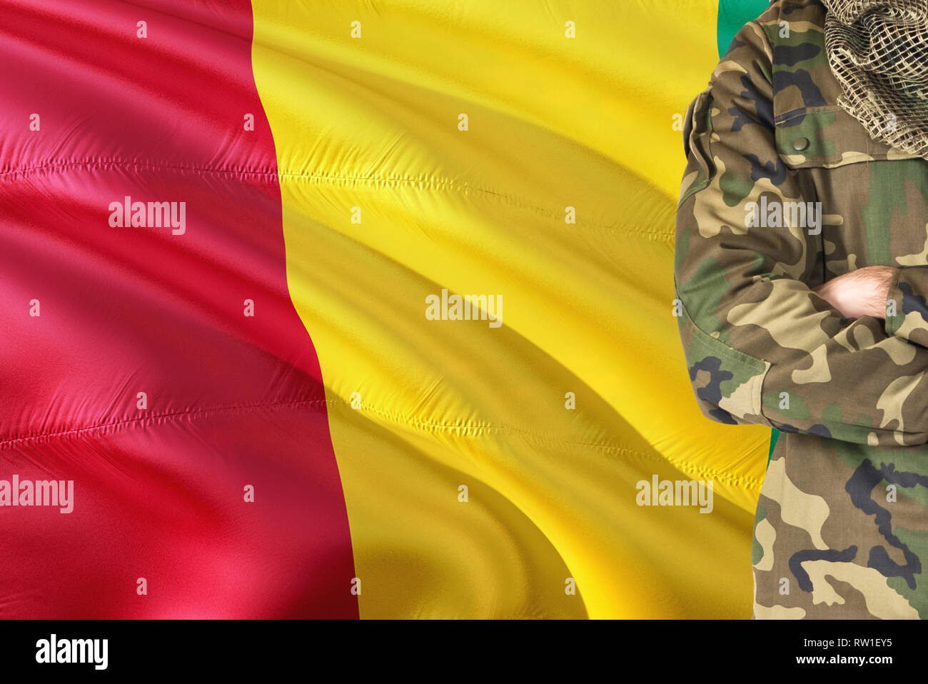 Crossed arms Guinean soldier with national waving flag on background ...